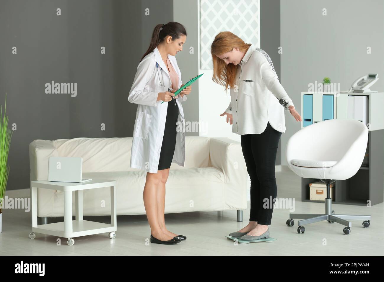 Young female doctor measuring weight of overweight woman in clinic ...