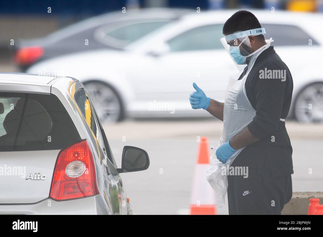 A tester wearing personal protective equipment (PPE) gestures to a ...