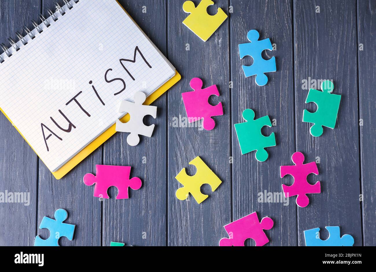 Word AUTISM written in notebook and puzzles on wooden background Stock ...