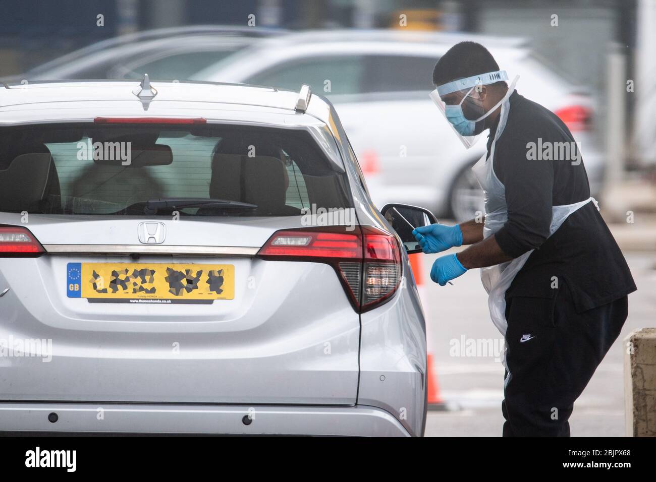 A tester wearing personal protective equipment (PPE) holds a test swab ...