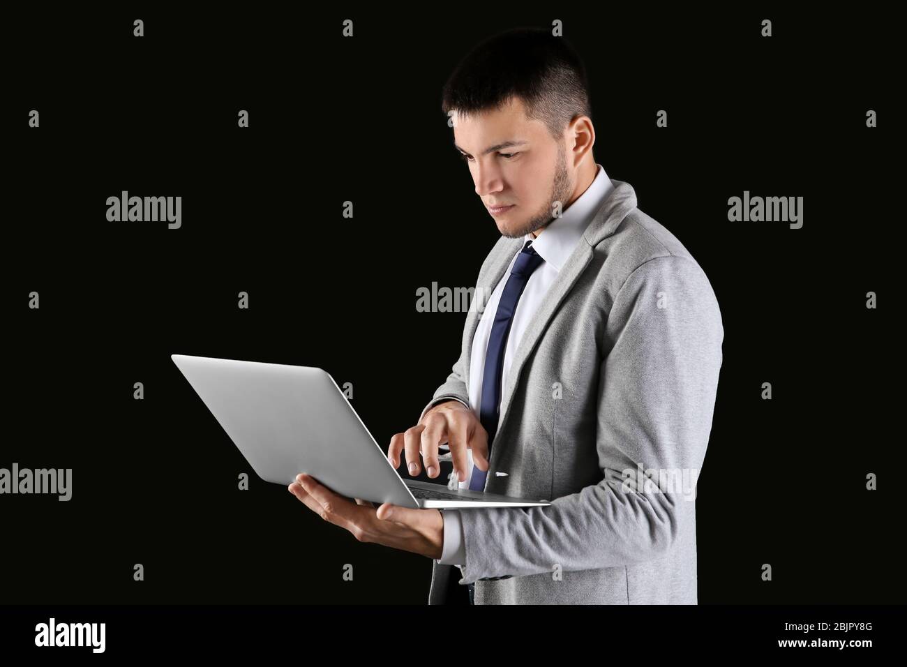 Man in formal suit with laptop on black background Stock Photo - Alamy