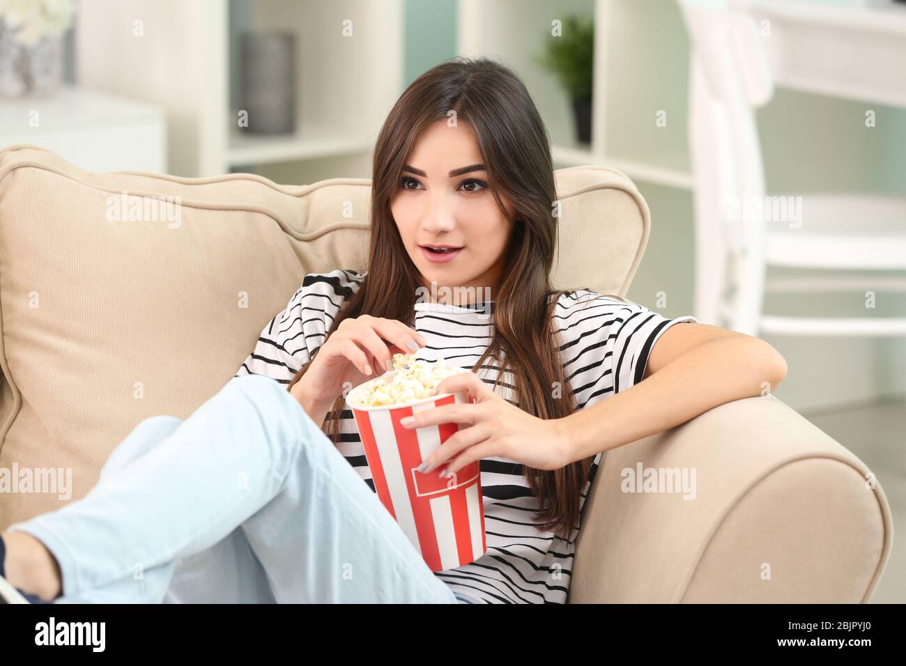 Young woman eating popcorn on sofa at home Stock Photo - Alamy