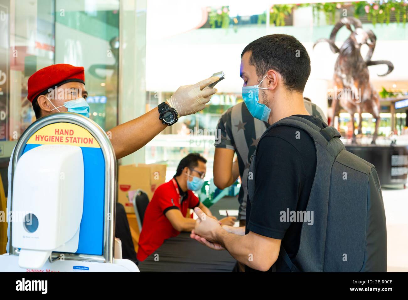 A security guard at the entrance to the mall measures the temperature ...