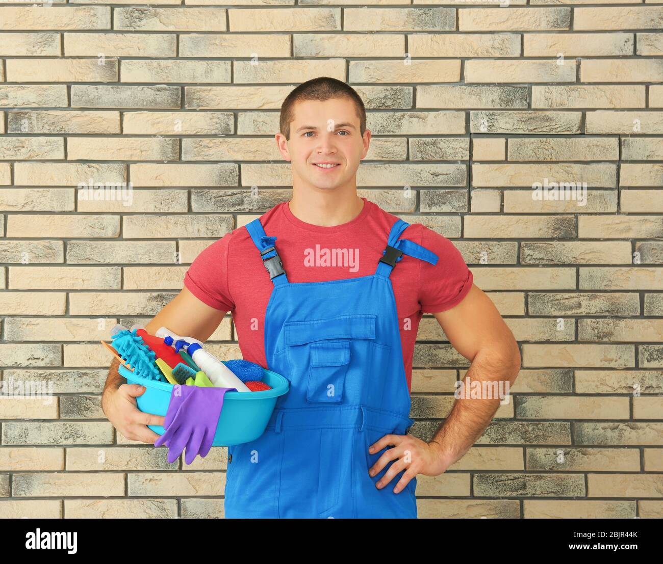 Young man with cleaning supplies on brick wall background Stock Photo ...