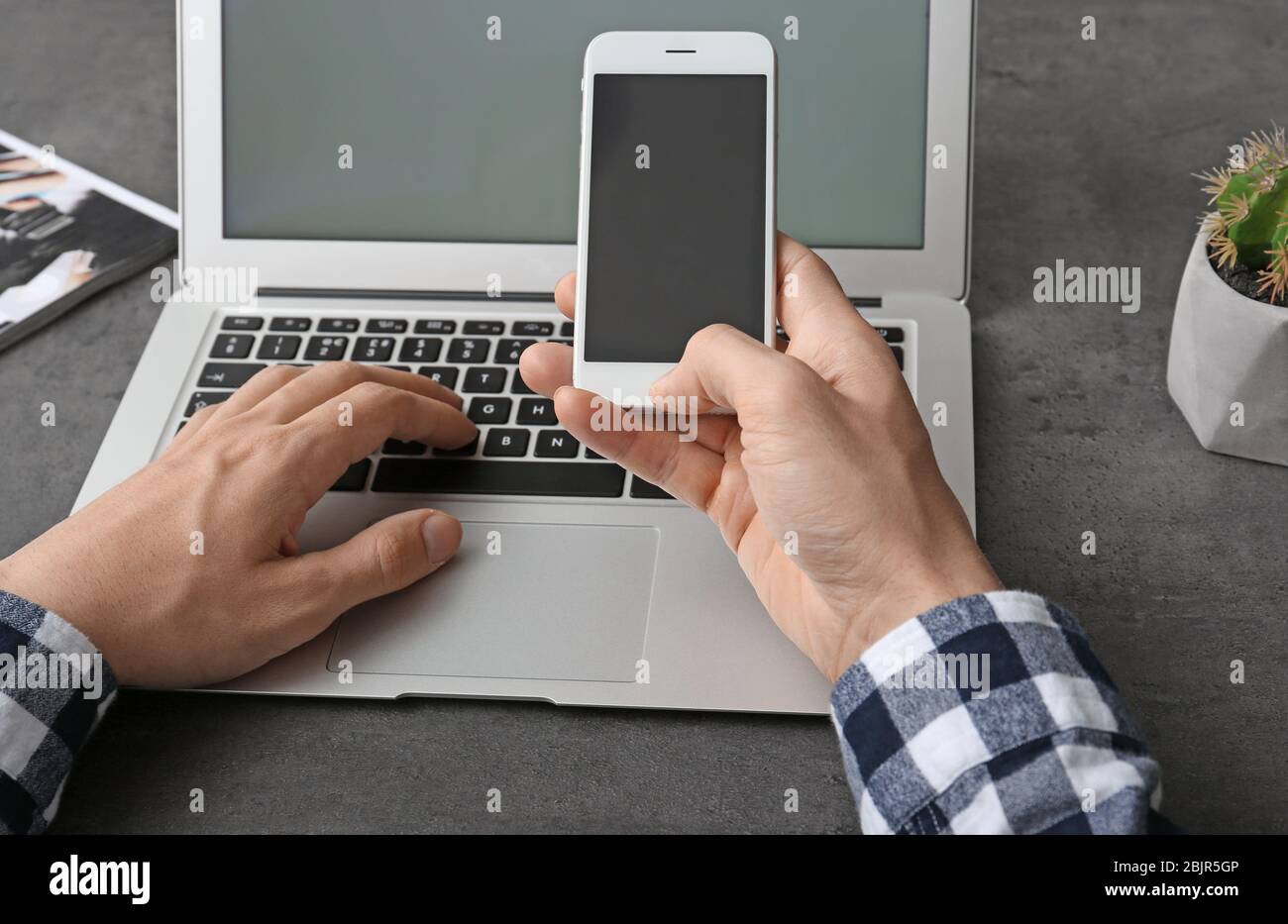 Man using cell phone and laptop on table Stock Photo - Alamy