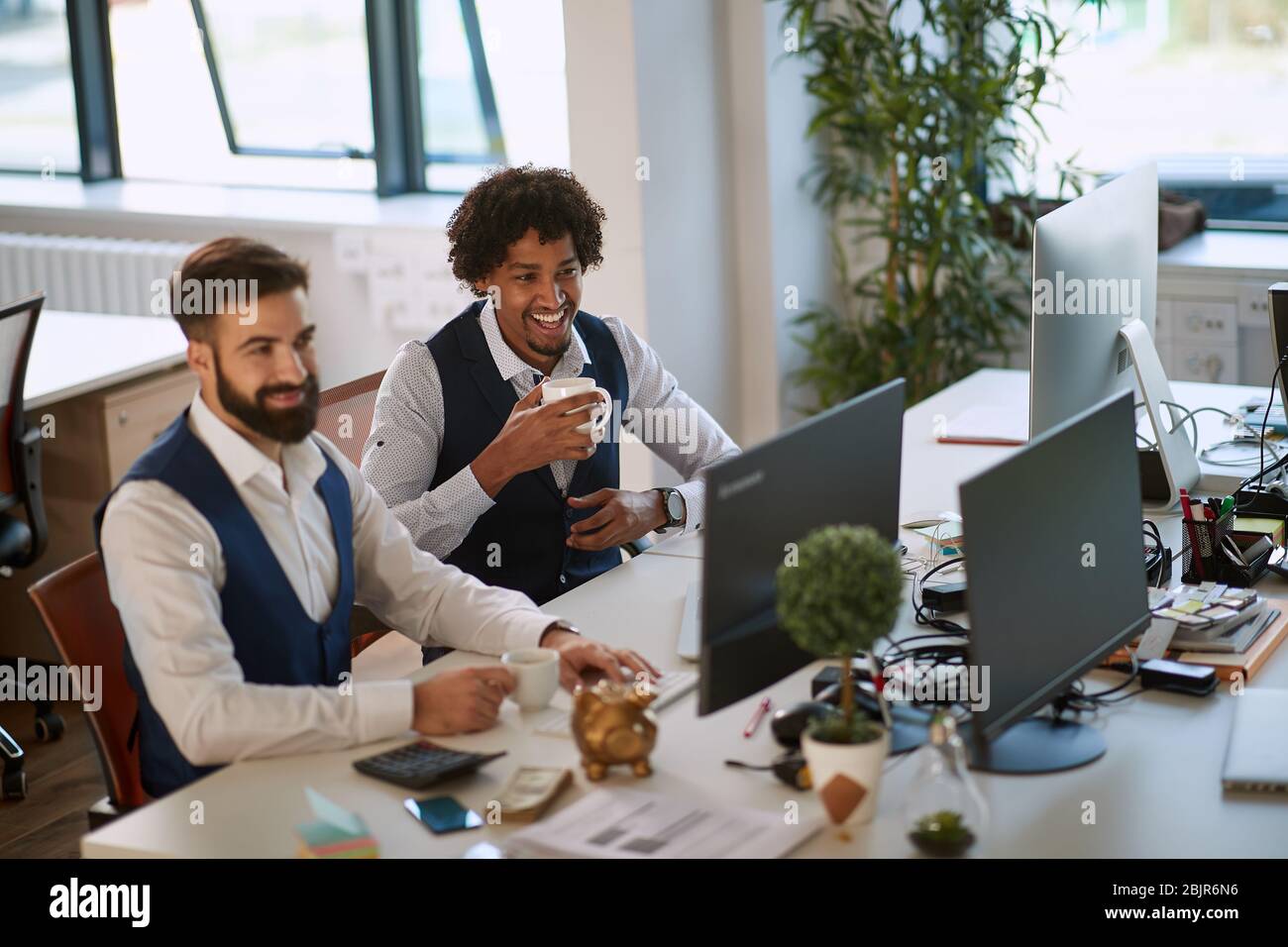 colleagues watching content on computer monitor at workplace, laughing ...
