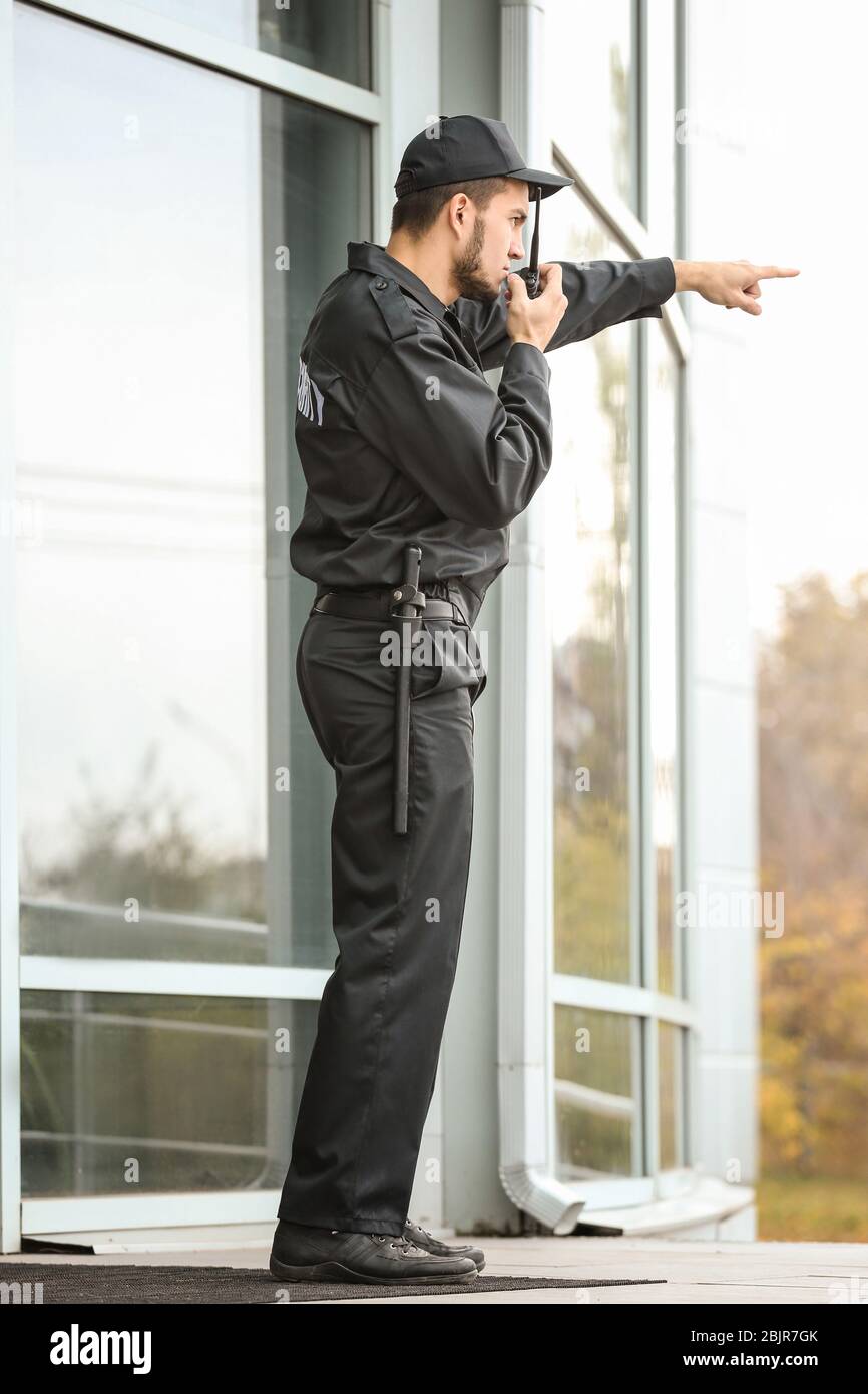 Male security guard using portable radio transmitter near building ...