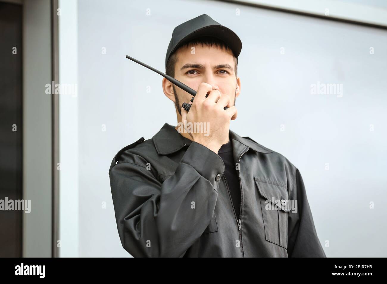 Male security guard using portable radio transmitter near building ...