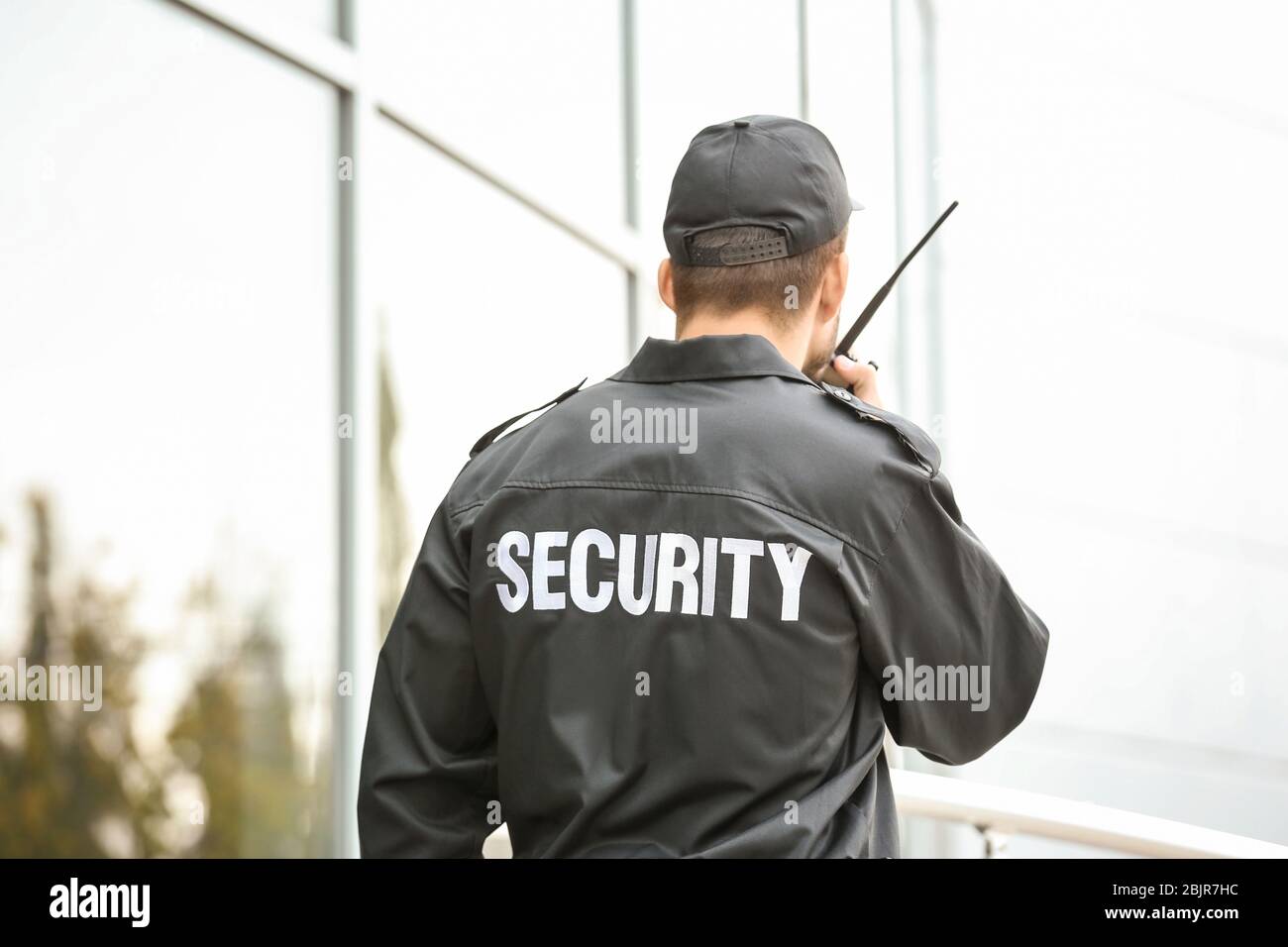 Male security guard using portable radio transmitter near building ...