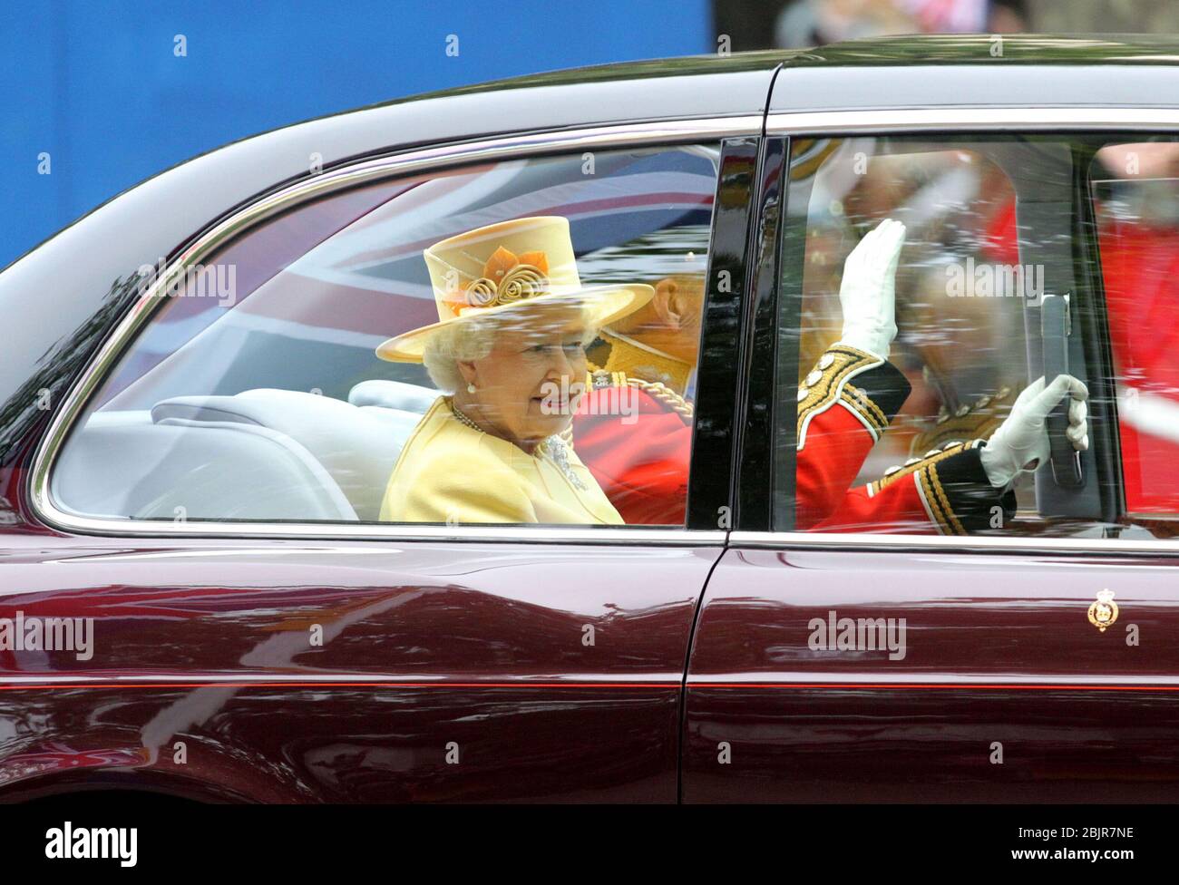 A smiling and waving HRH Queen Elizabeth II dressed in yellow & The ...