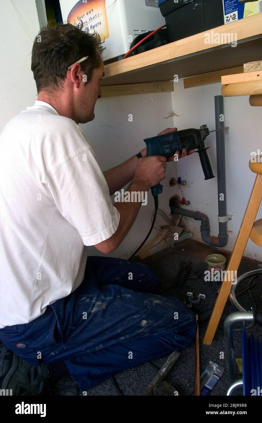 Plumber plumbing in washing machine in kitchen in north east England ...