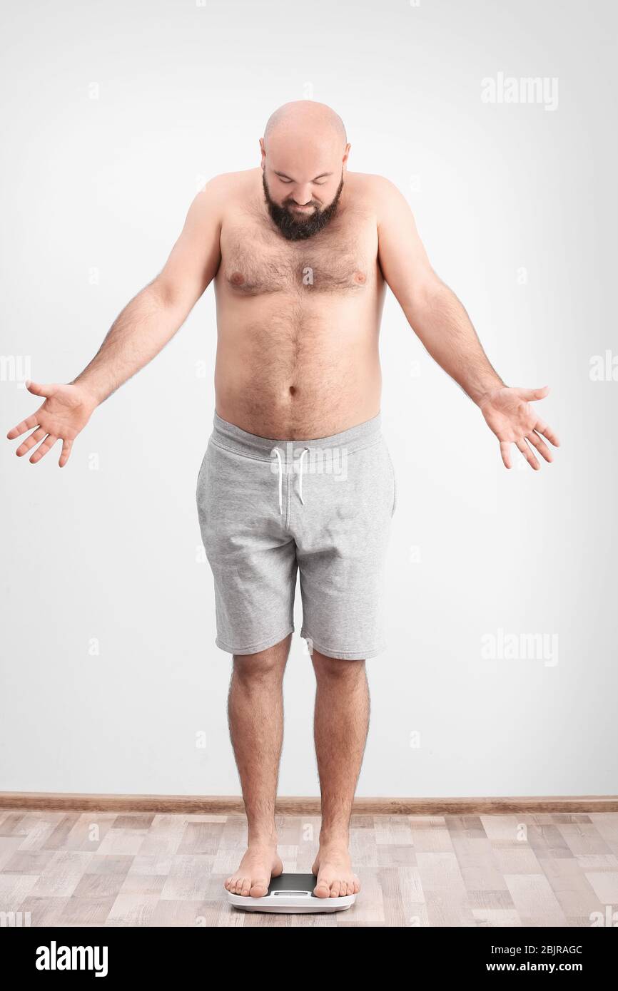 Overweight man measuring his weight using scales on floor Stock Photo ...