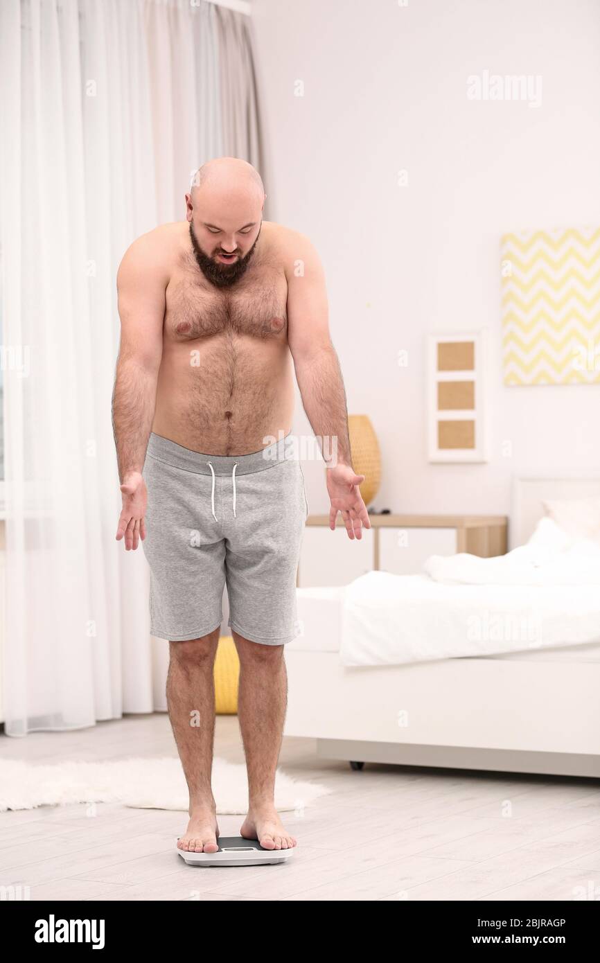 Overweight man measuring his weight using scales at home Stock Photo ...