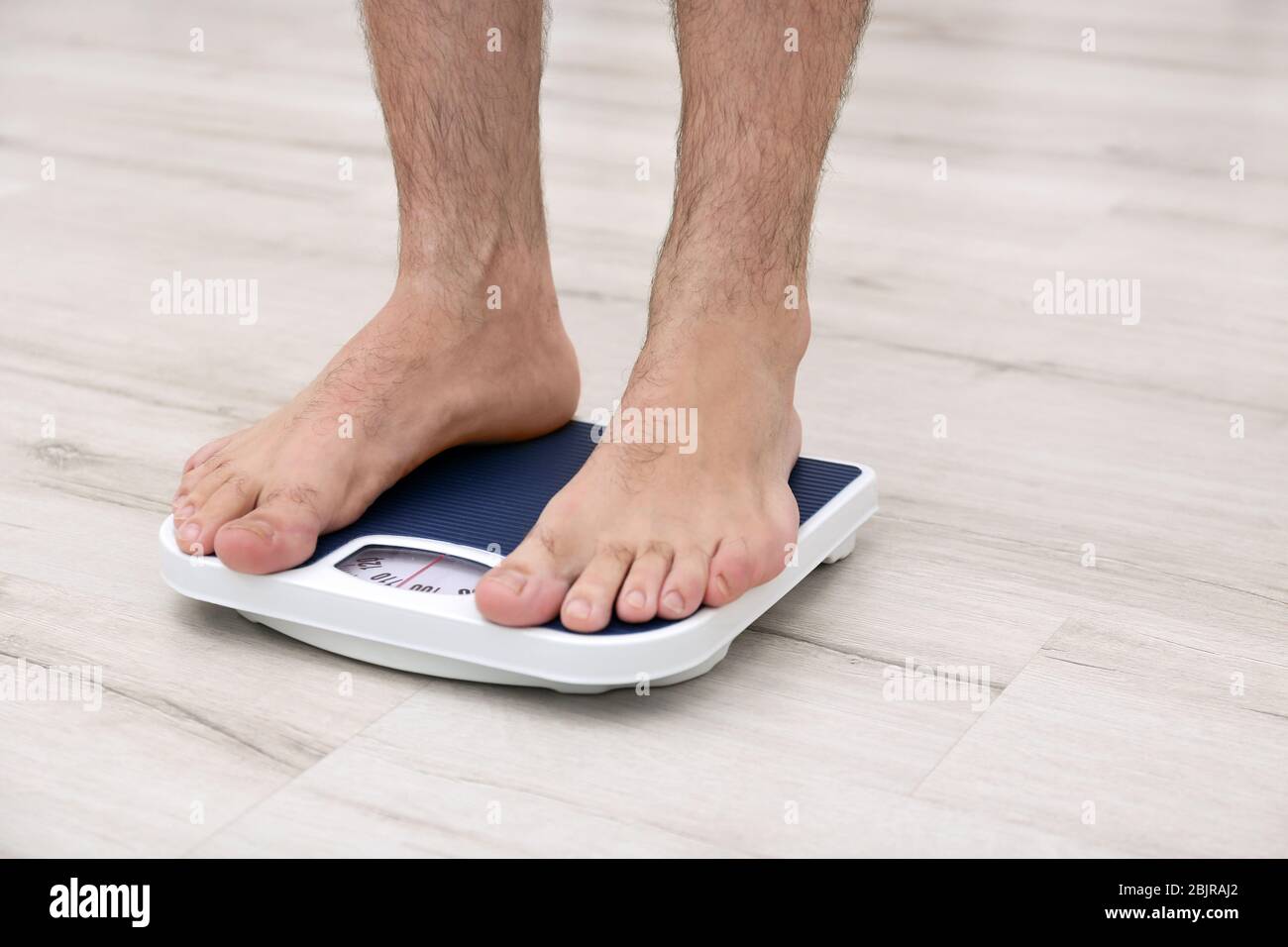 Overweight man measuring his weight using scales on floor Stock Photo ...