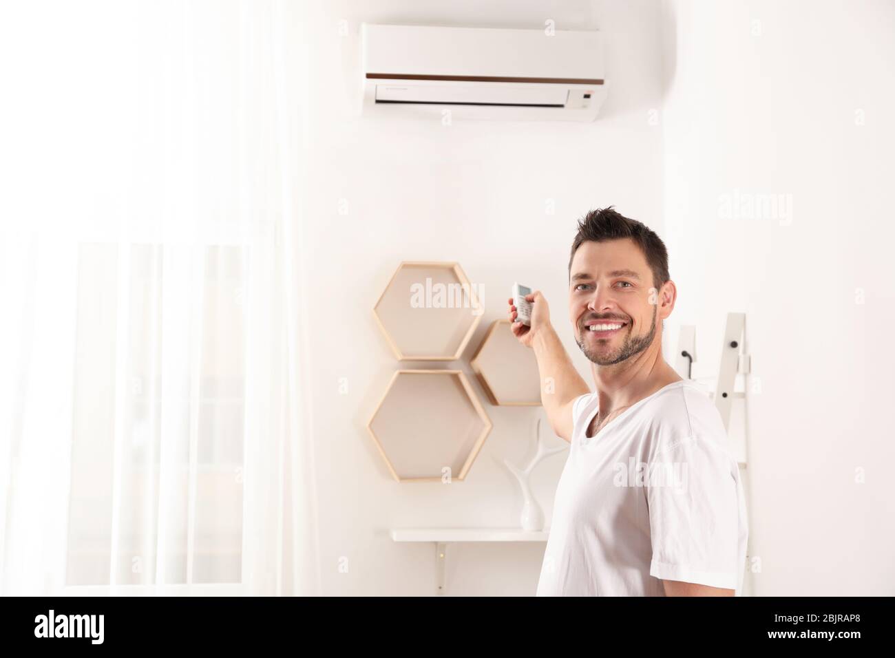 Handsome man switching on air conditioner at home Stock Photo - Alamy