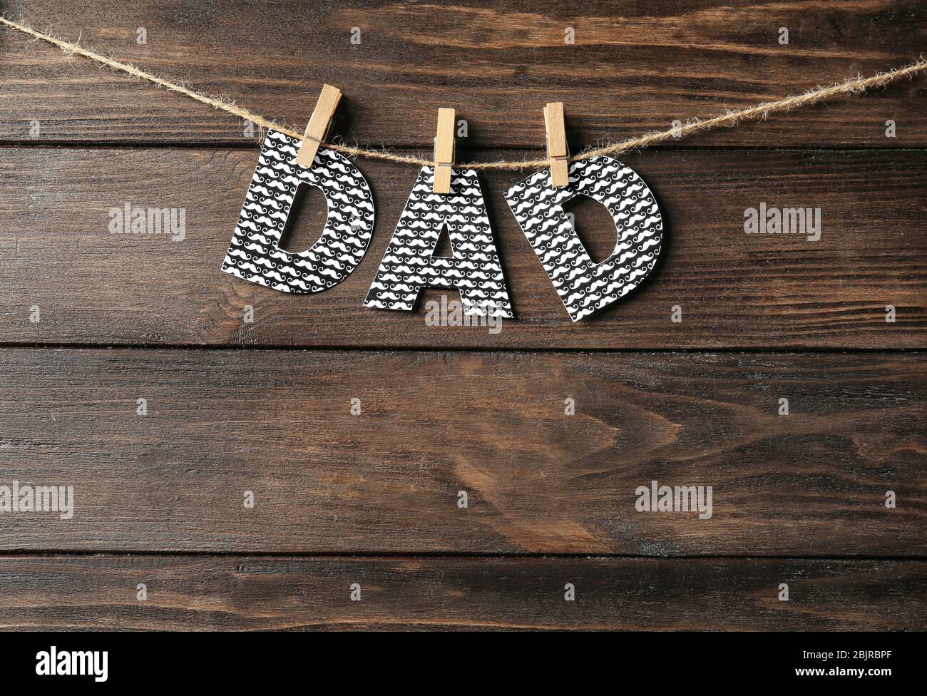 Word DAD made of paper letters hanging on rope against wooden ...