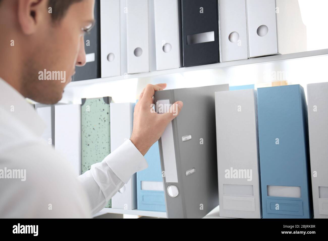 Young man taking folder with documents from shelf in archive Stock ...