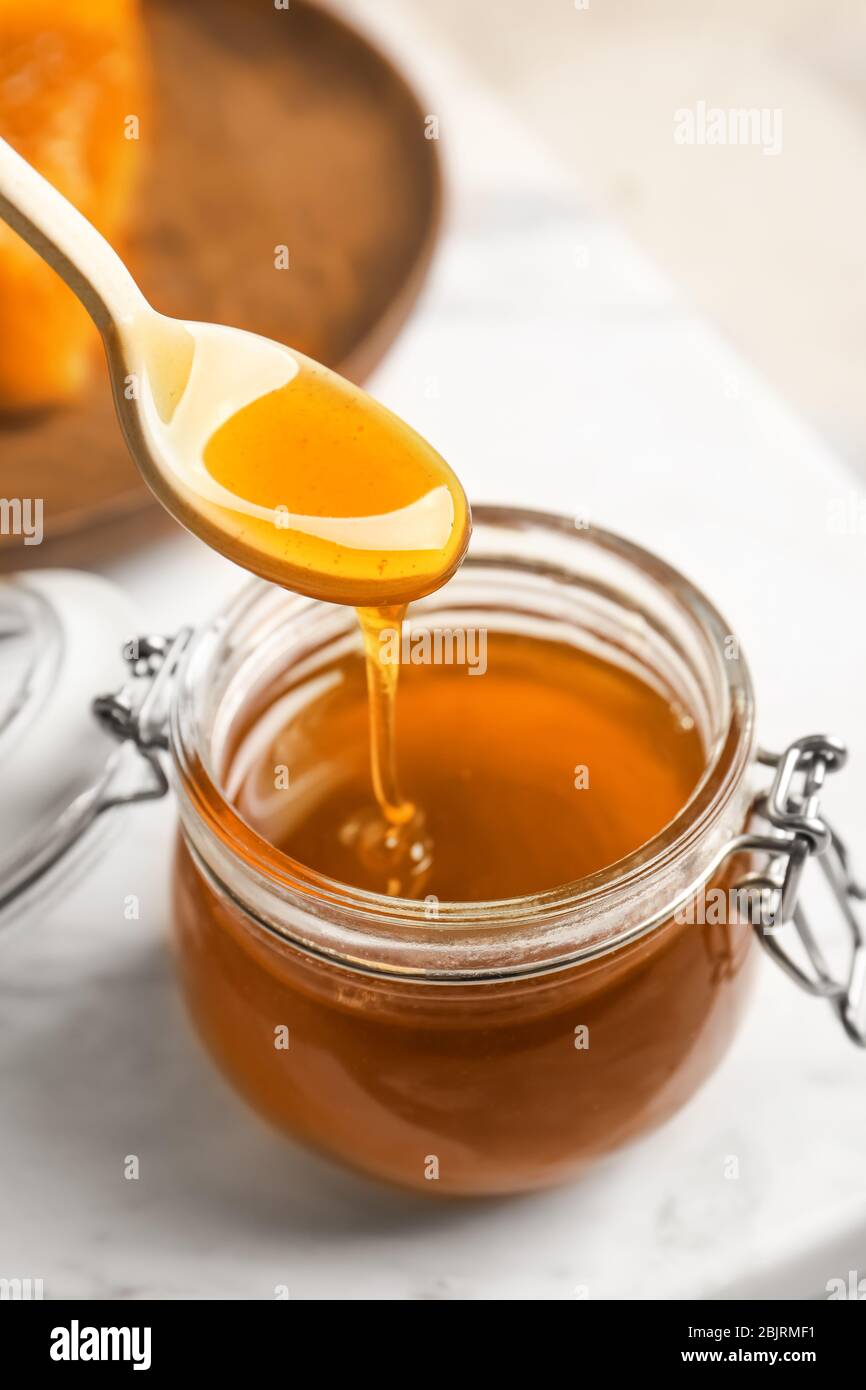 Honey pouring from wooden spoon into glass jar, closeup Stock Photo - Alamy