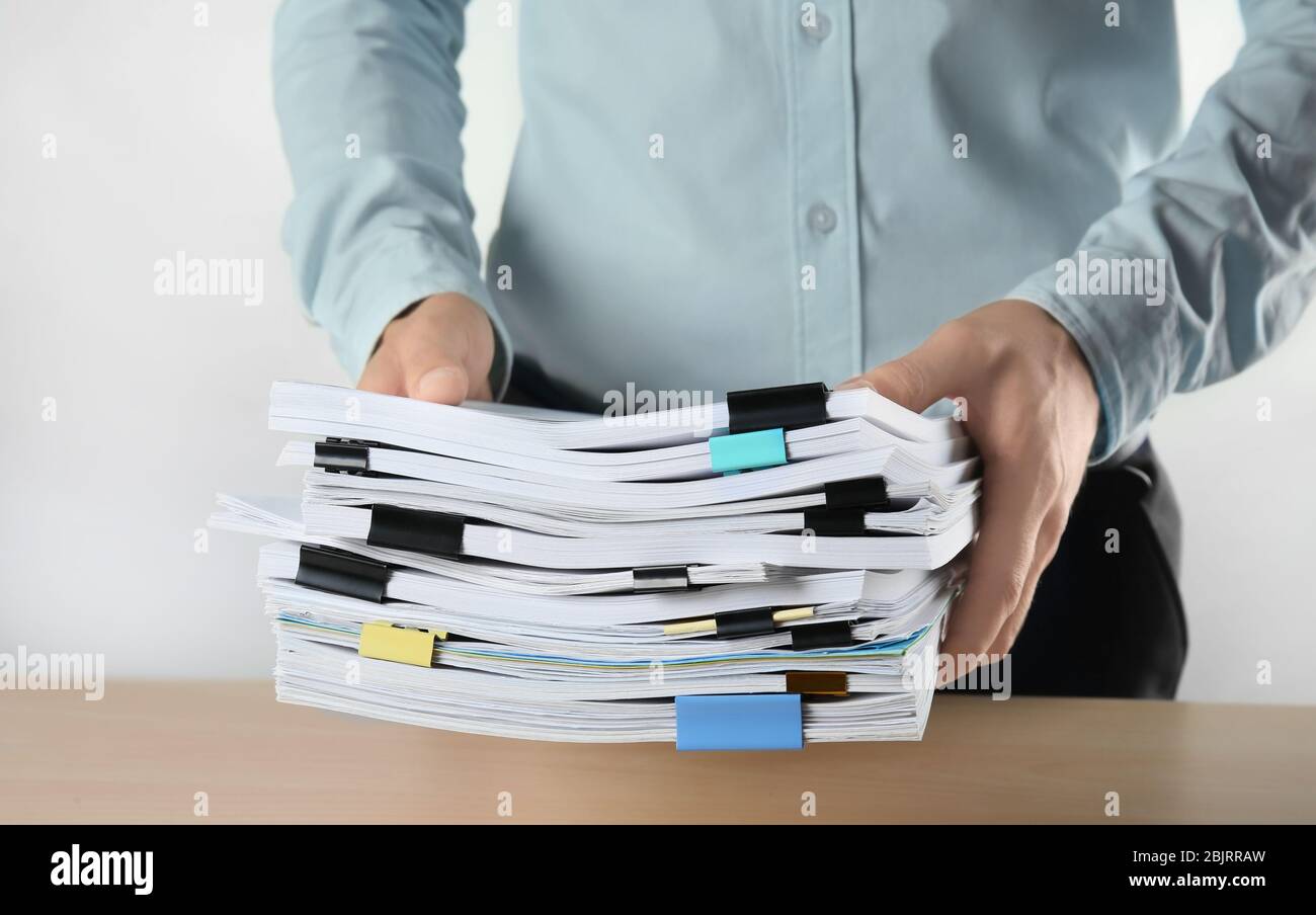 Man with stack of documents against light background Stock Photo - Alamy