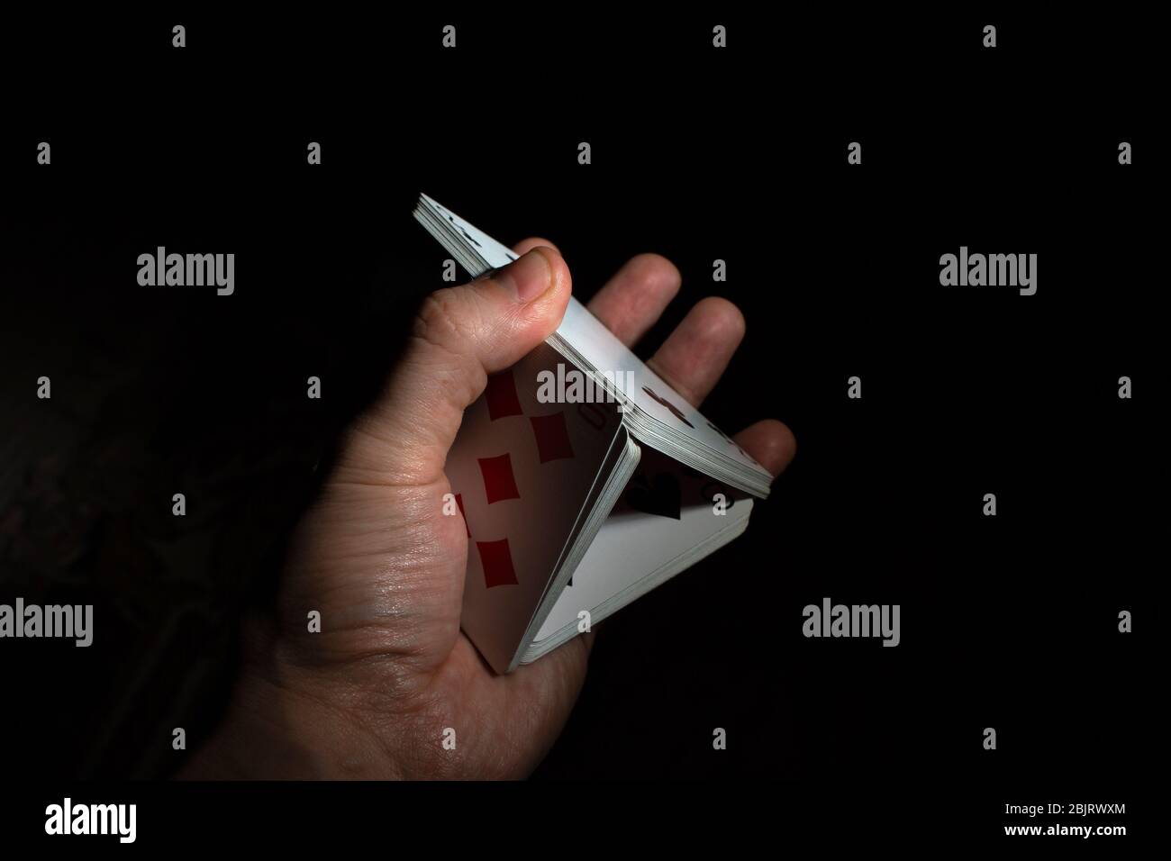 hand hold a triangle from a deck of poker cards on a black background ...