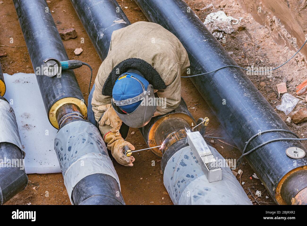 Welder worker welds new metal pipe on the construction site Stock Photo ...