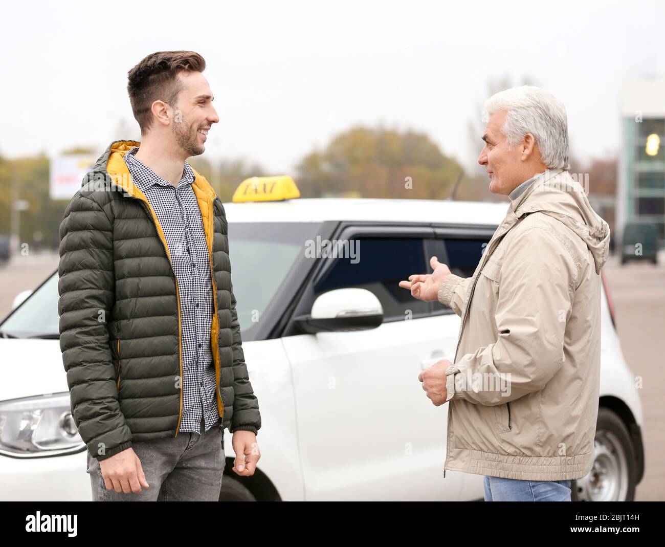 Young trainee and senior driver talking near taxi car Stock Photo - Alamy