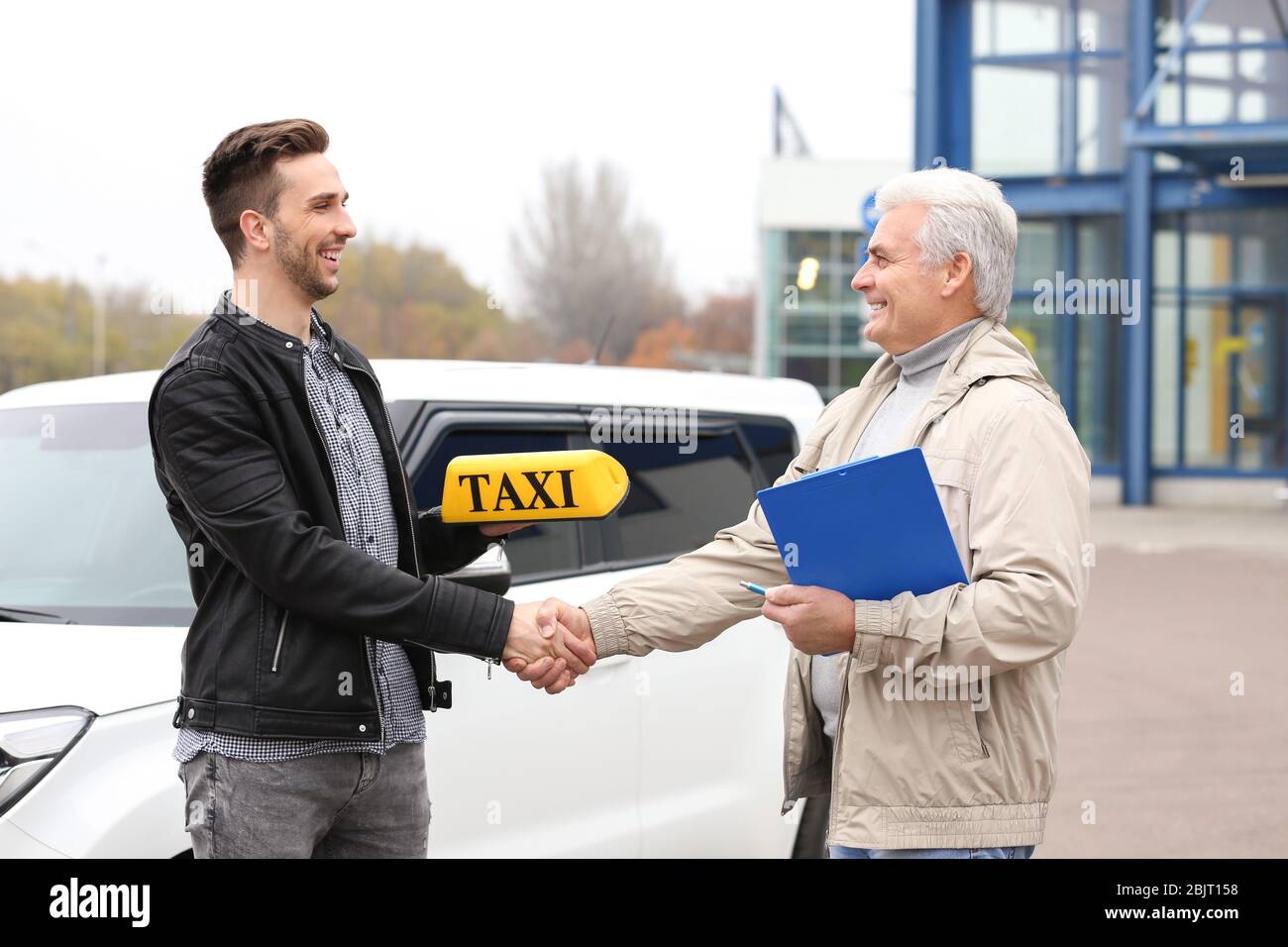 Young trainee shaking hands with senior taxi driver outdoors Stock ...