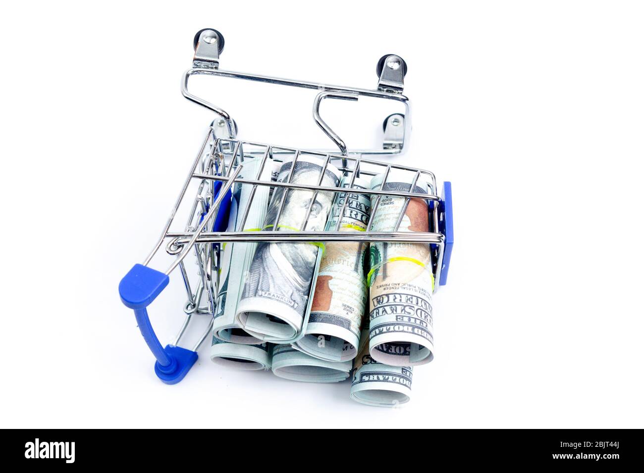fallen shopping cart with rolls of one hundred dollar bills on a white ...