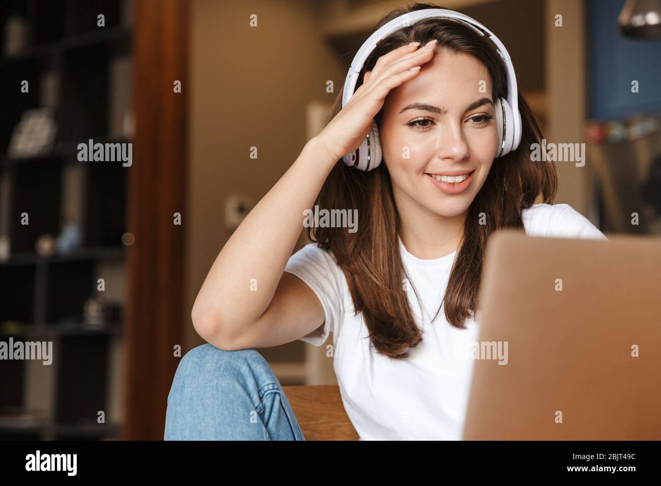 Photo of a young cheerful woman indoors at home using laptop computer ...