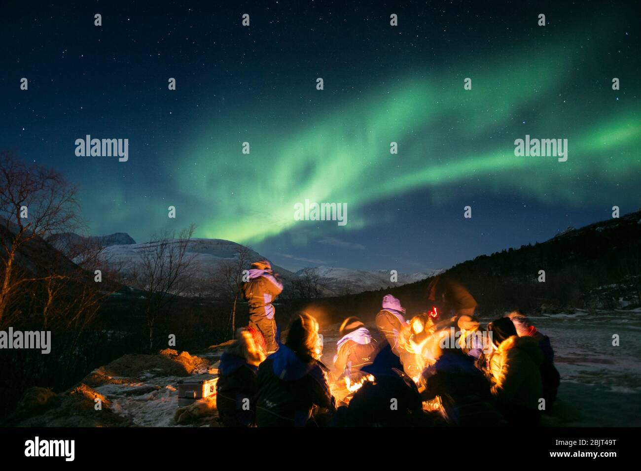 Group of people huddled around a campfire with the northern lights ...