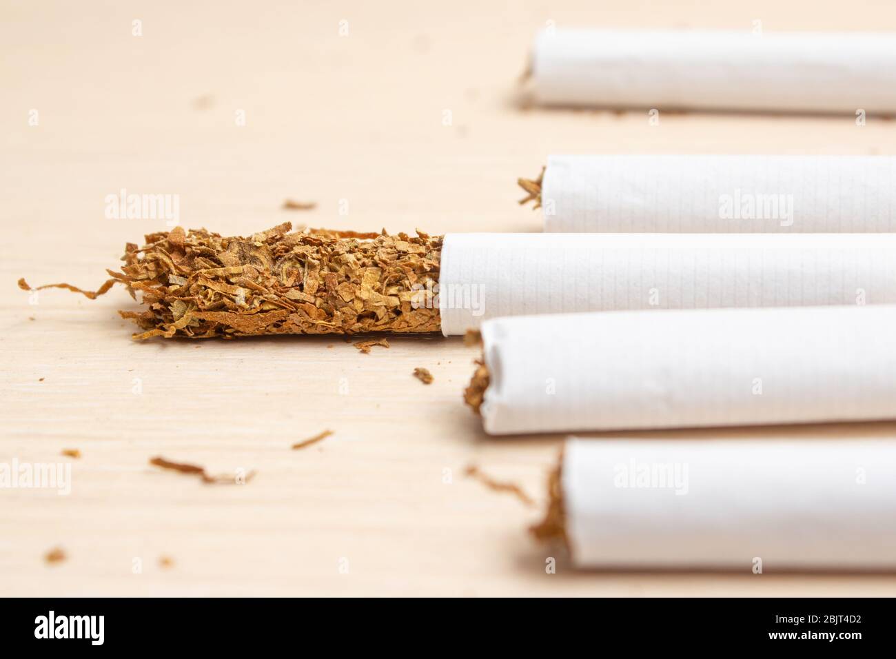 five cigarettes and one got out on half tobacco on a light wooden Stock ...