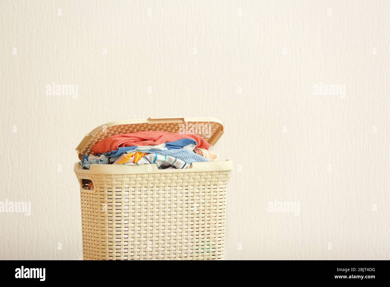Plastic laundry basket with clothes on light background Stock Photo - Alamy