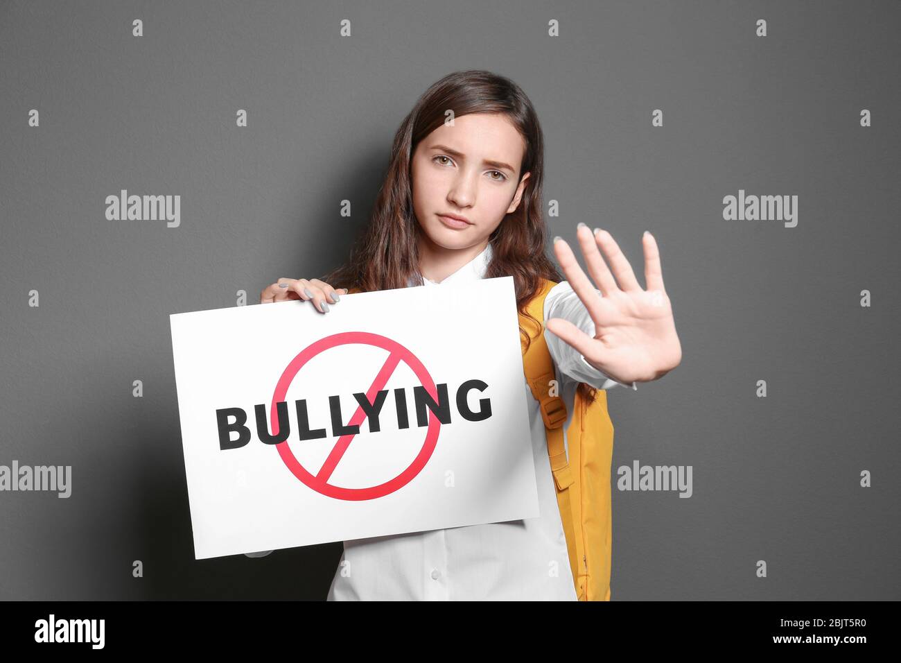 Teenage girl holding sign with crossed word "Bullying" on grey ...
