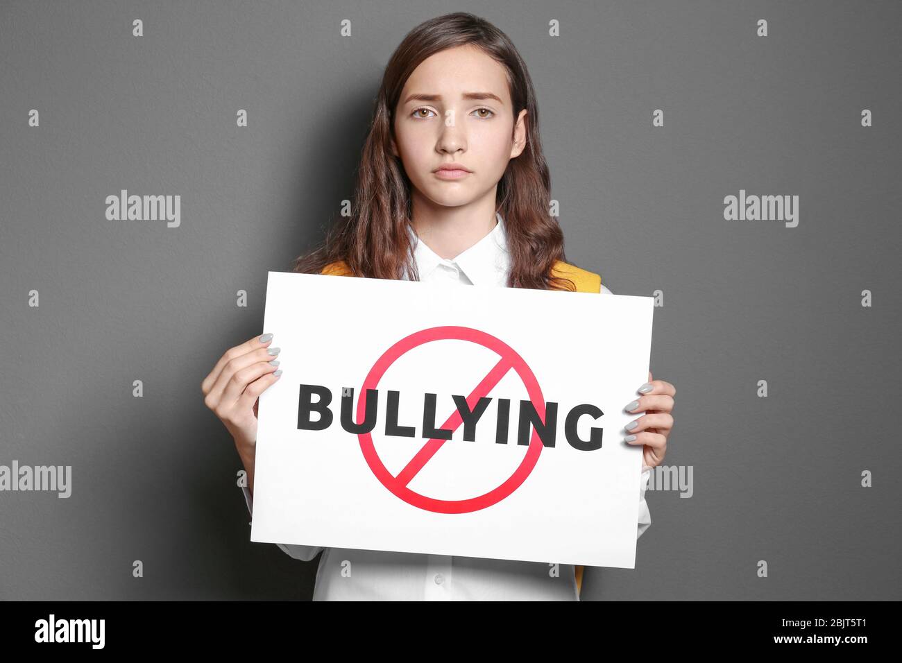 Teenage girl holding sign with crossed word "Bullying" on grey ...