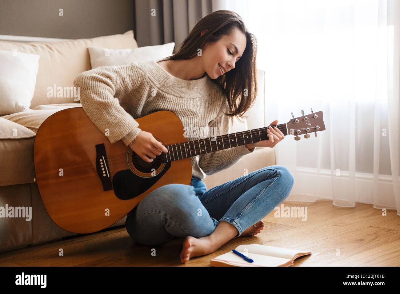 Image of happy beautiful woman playing guitar and composing song while ...