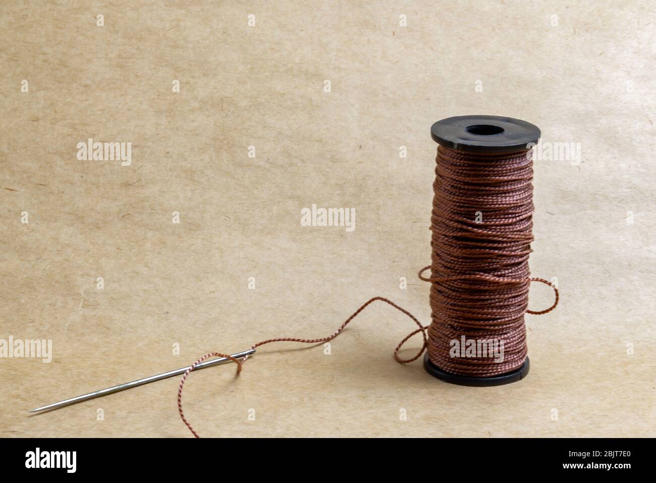brown thread with a needle on a cardboard background Stock Photo - Alamy