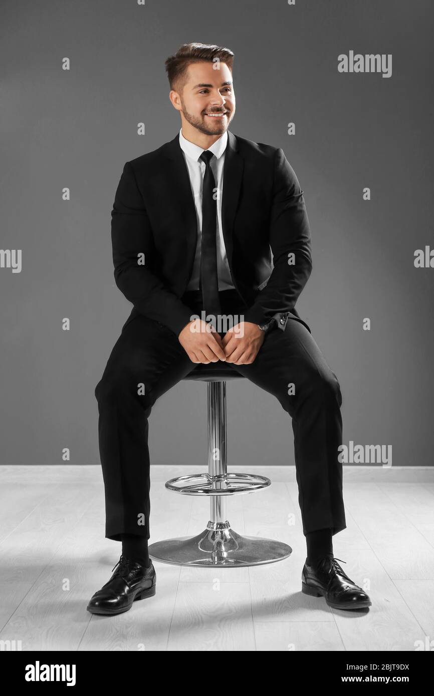 Handsome man in formal suit sitting on chair against grey wall Stock ...