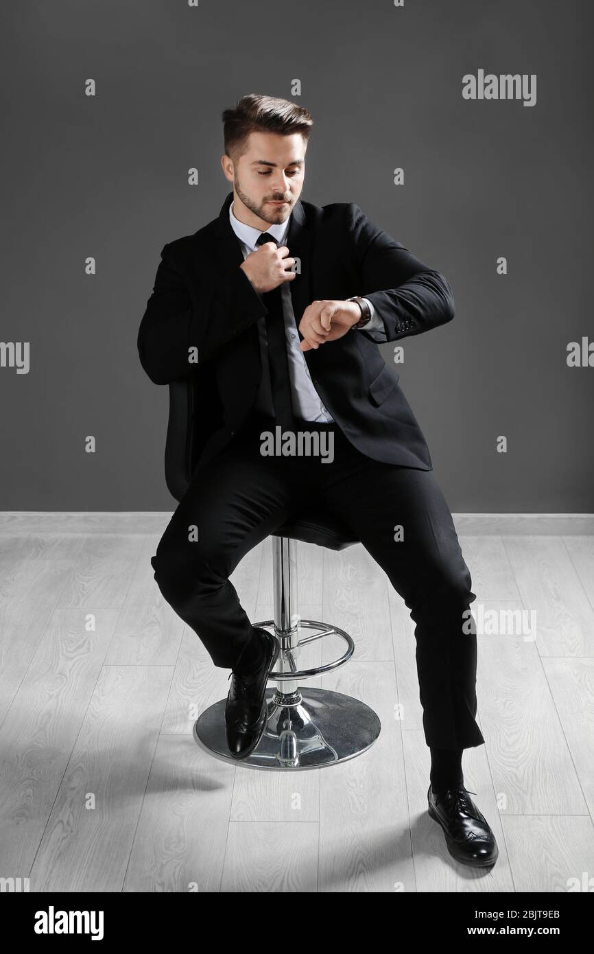 Handsome man in formal suit sitting on chair against grey wall Stock ...