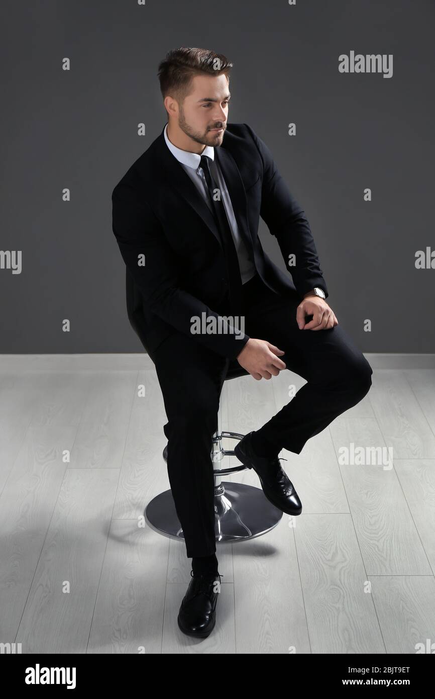 Handsome man in formal suit sitting on chair against grey wall Stock ...