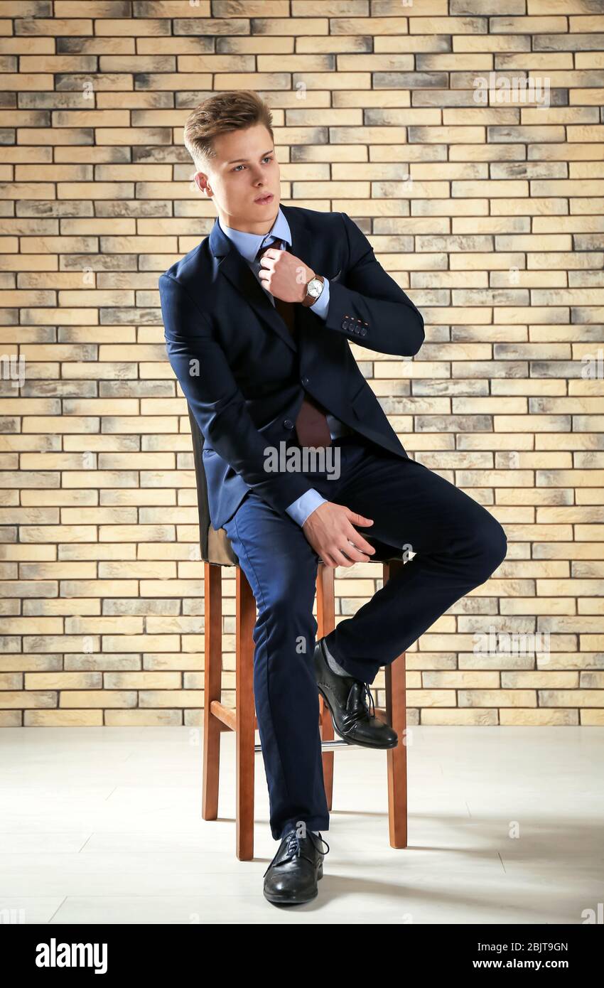 Handsome man in formal suit sitting on chair against brick wall Stock ...