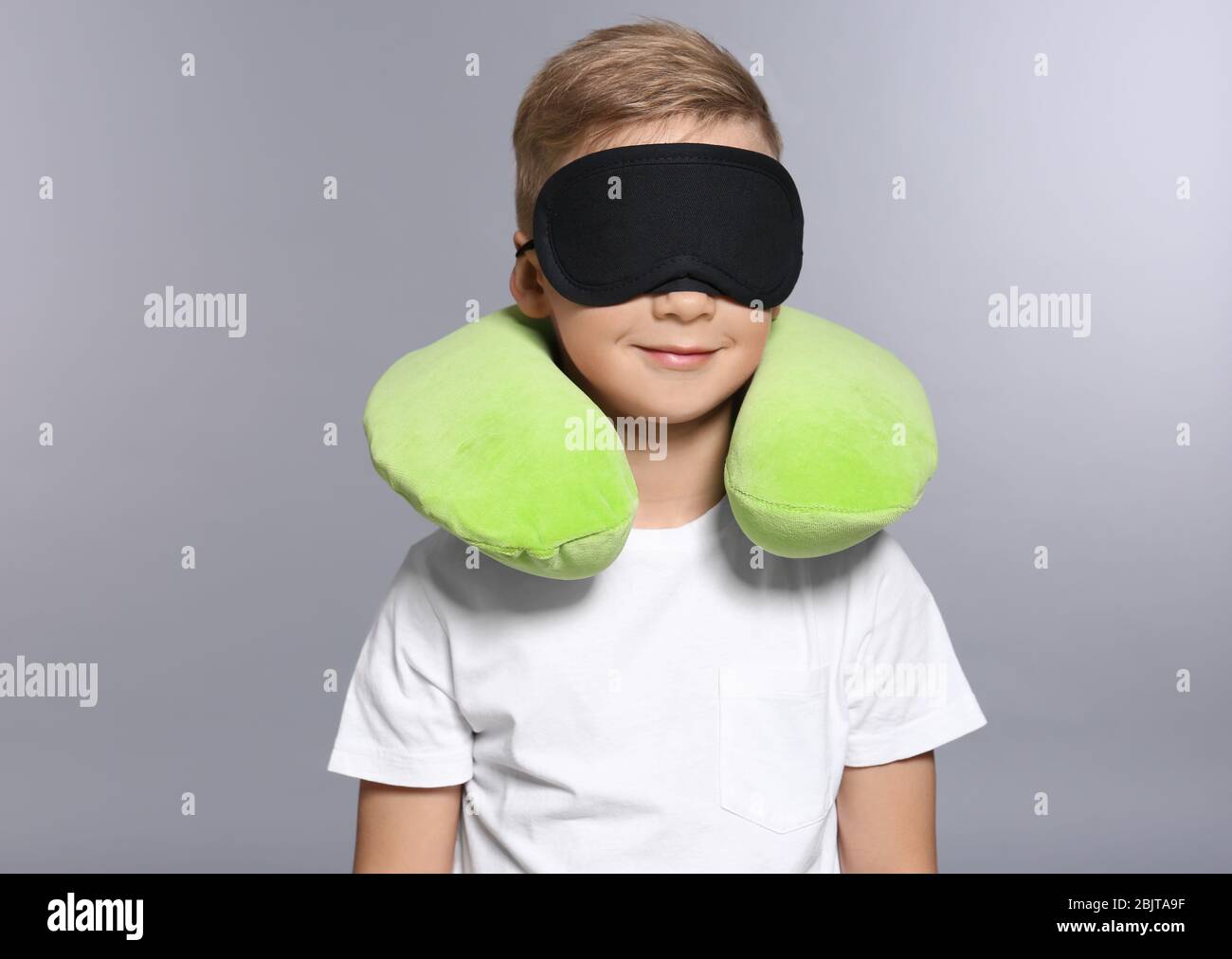 Cute boy with travel pillow and sleep mask on grey background Stock ...