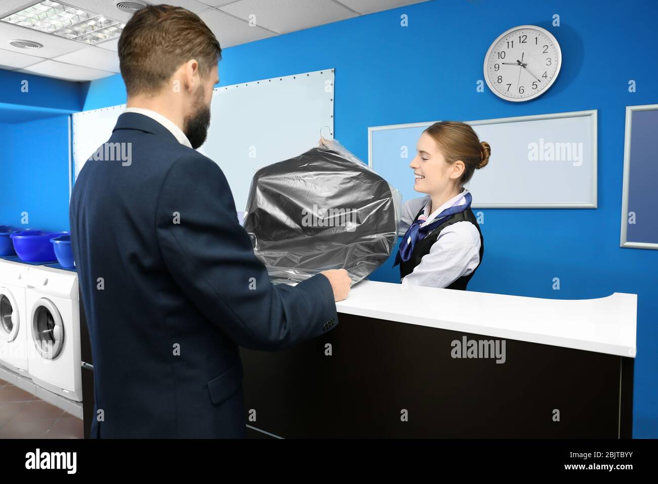 Young man receiving his clean suit from laundry worker at reception ...