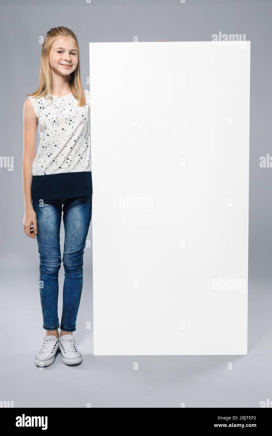 Cute girl with blank advertising board on grey background Stock Photo ...