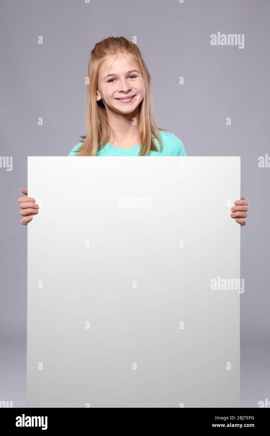 Cute girl with blank advertising board on grey background Stock Photo ...