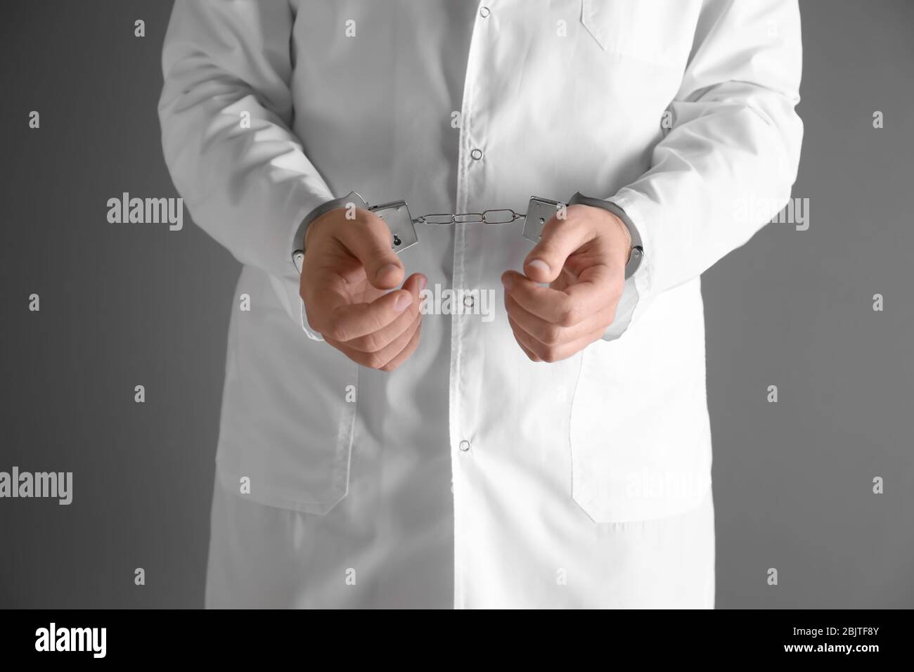 Male doctor in handcuffs on black background Stock Photo - Alamy