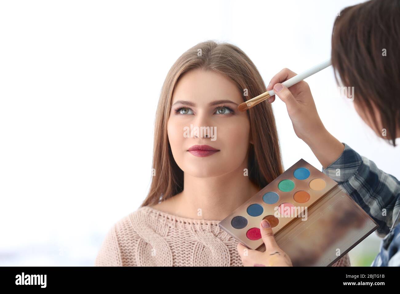 Professional artist creating makeup for beautiful model on light ...