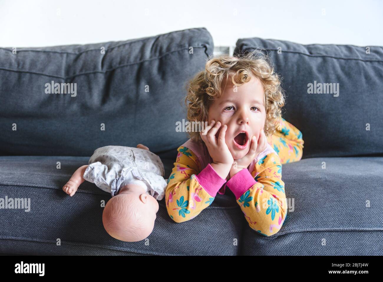 small bored blonde girl laying on a grey sofa Stock Photo - Alamy