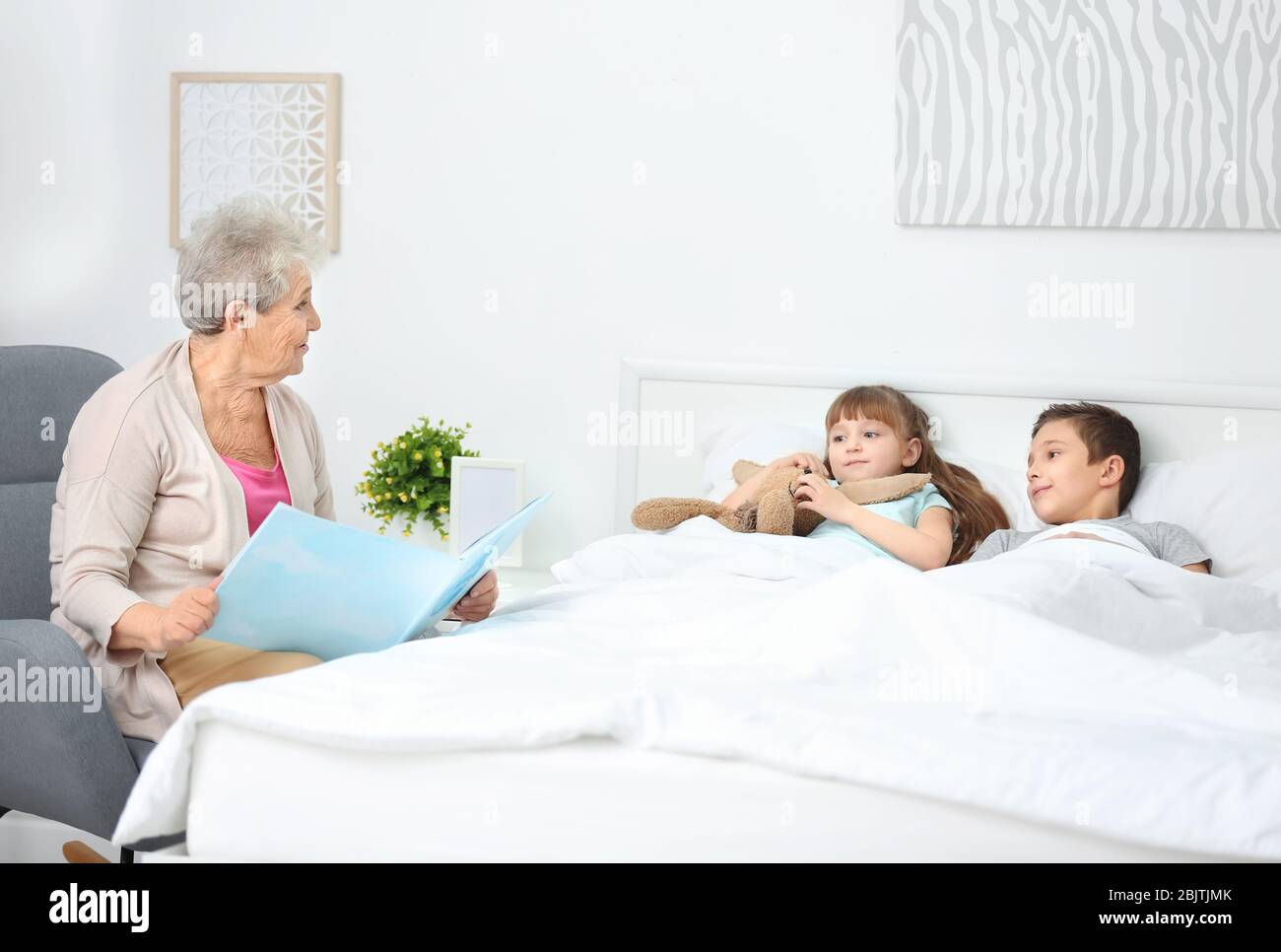 Senior nanny reading book to little children in bedroom Stock Photo - Alamy