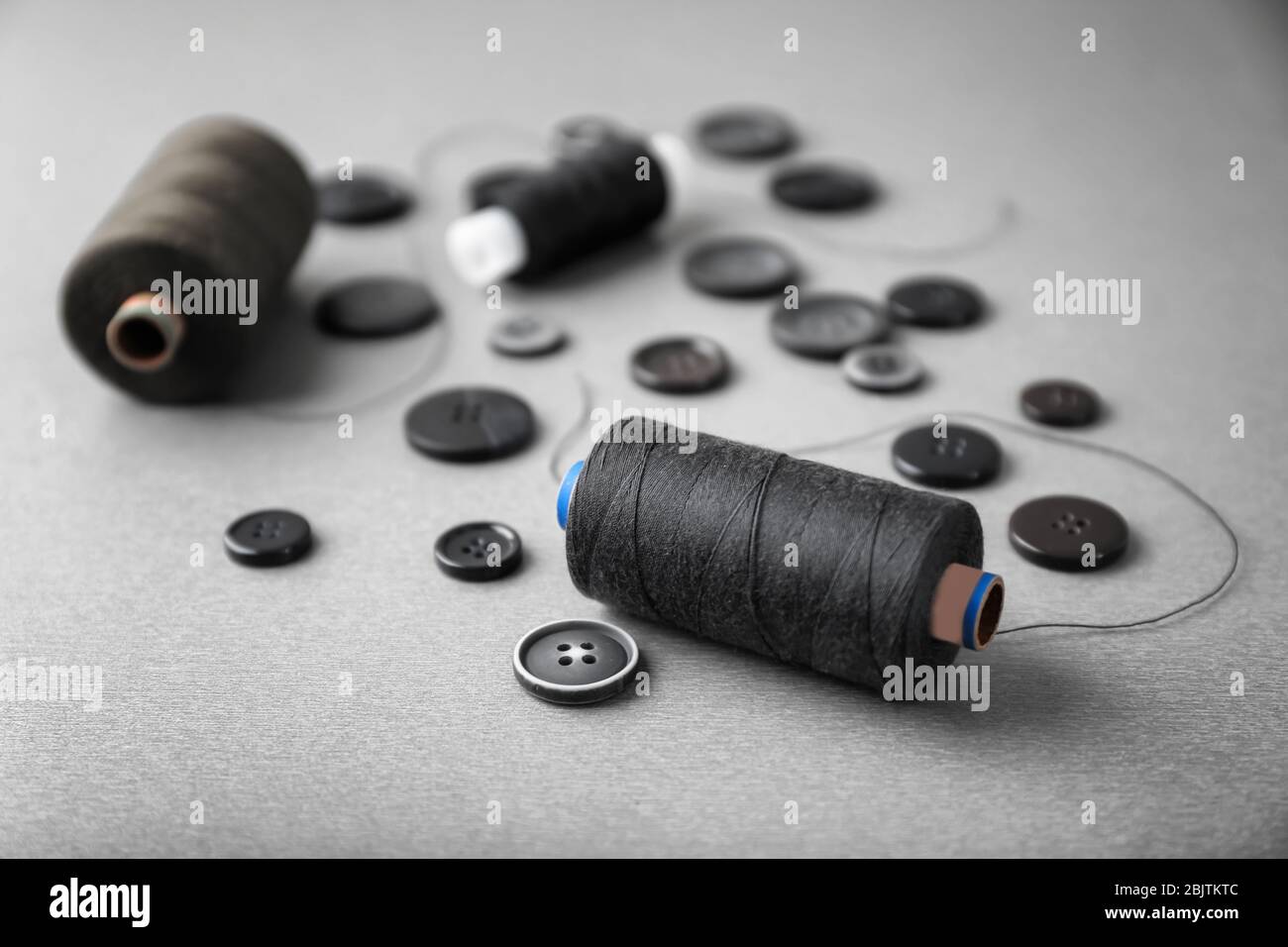 Dark sewing threads with buttons on grey background Stock Photo - Alamy