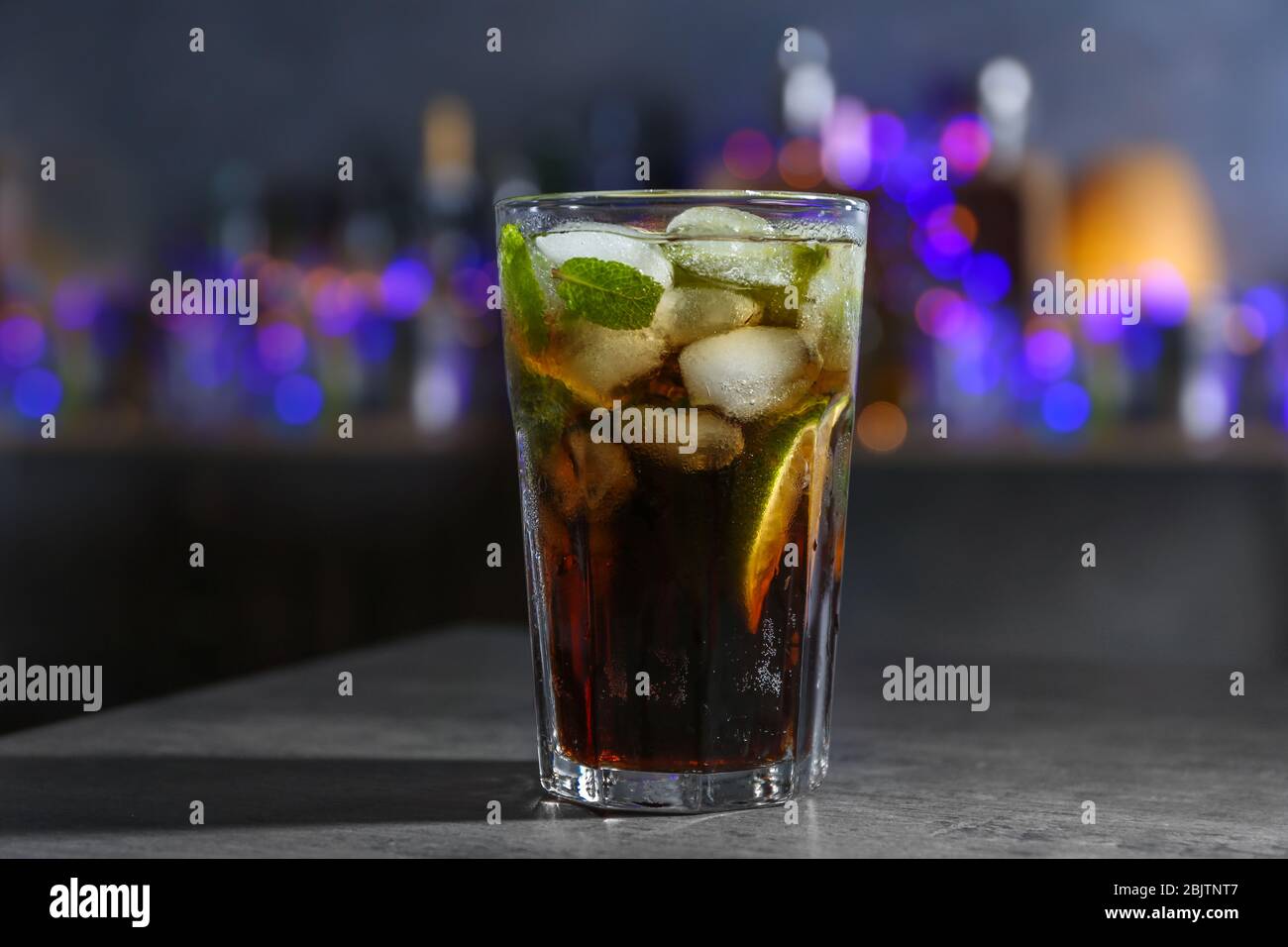 Glass with Cuba Libre cocktail on table against blurred background ...